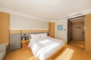 Quarto de hotel moderno com uma cama grande, uma mesa de cabeceira, um painel de controle na parede e uma porta para o banheiro.