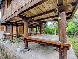 Uma estrutura de madeira ao ar livre com área de estar coberta, colunas e plantas em vasos.