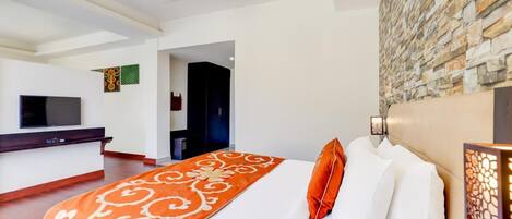 Quarto de hotel com cama, televisão de tela plana, escrivaninha e parede de pedra.