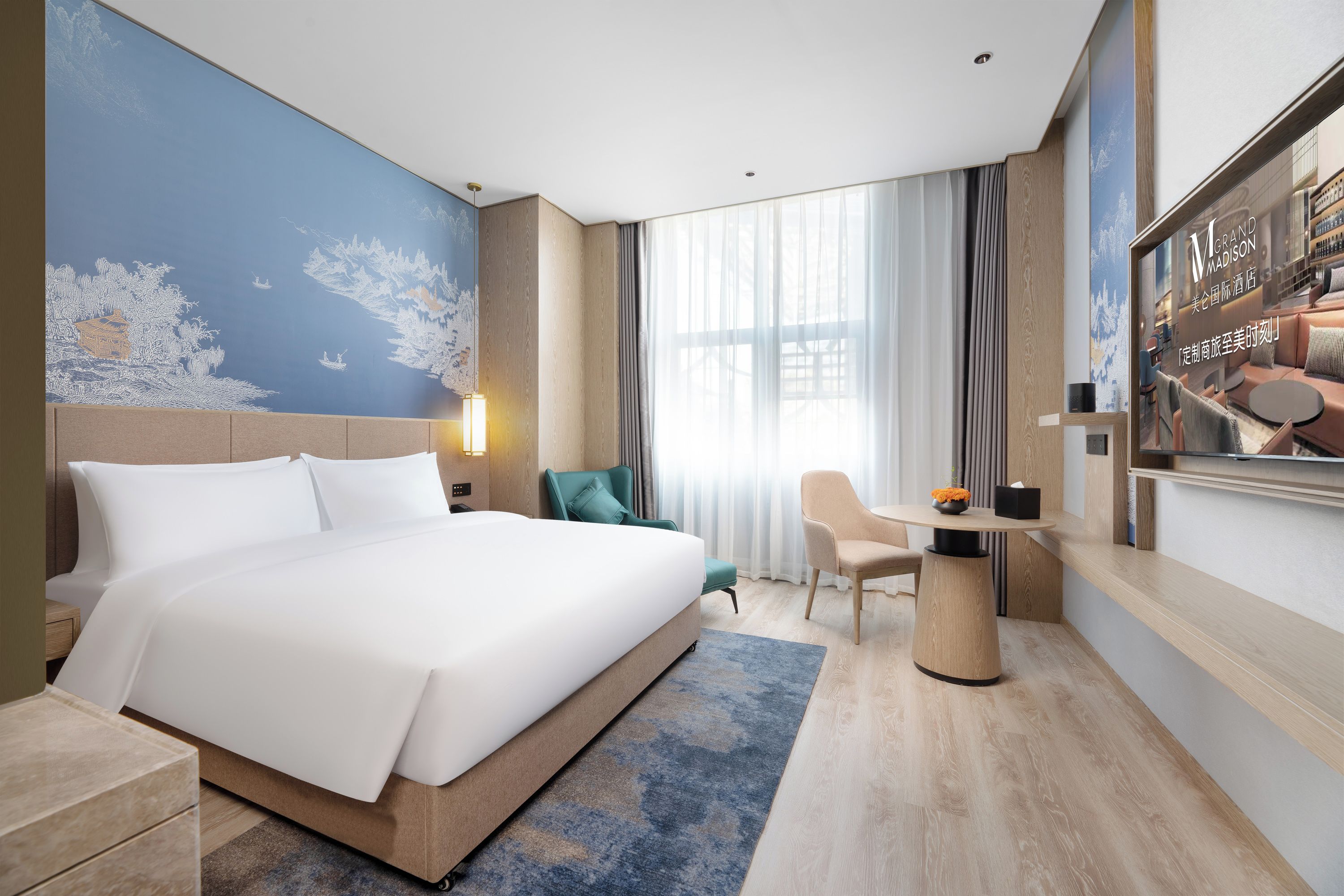 Quarto de hotel com cama grande, escrivaninha, cadeira, televisão e um mural na parede.