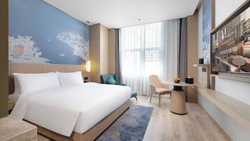Quarto de hotel com cama grande, escrivaninha, cadeira, televisão e um mural na parede.