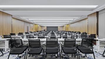 Uma sala de conferências com fileiras de mesas e cadeiras, equipada com computadores portáteis e garrafas de água.