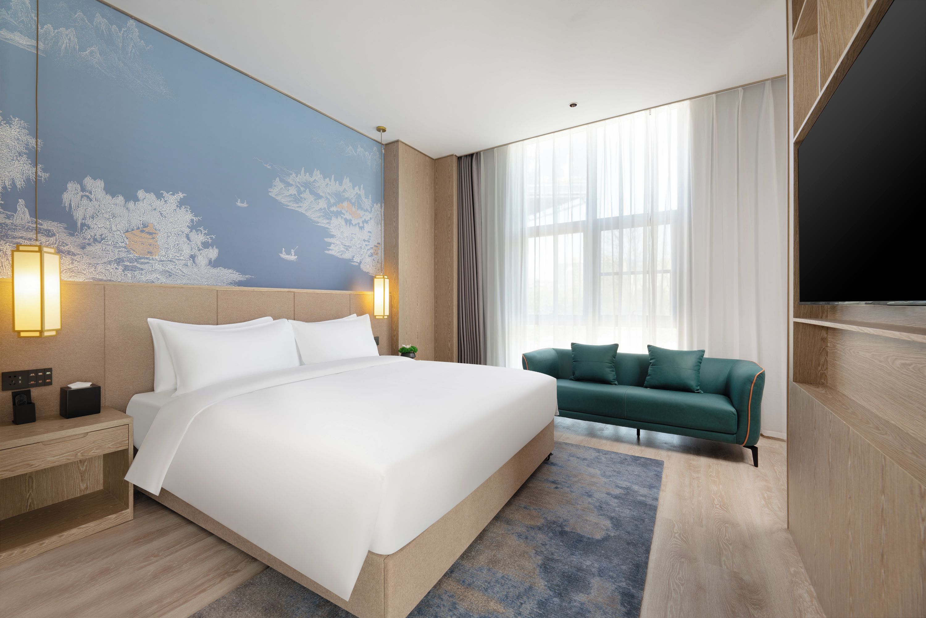 Quarto de hotel com cama grande, sofá, televisão e um mural na parede.