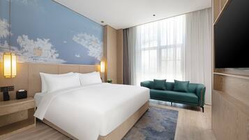 Quarto de hotel com cama grande, sofá, televisão e um mural na parede.