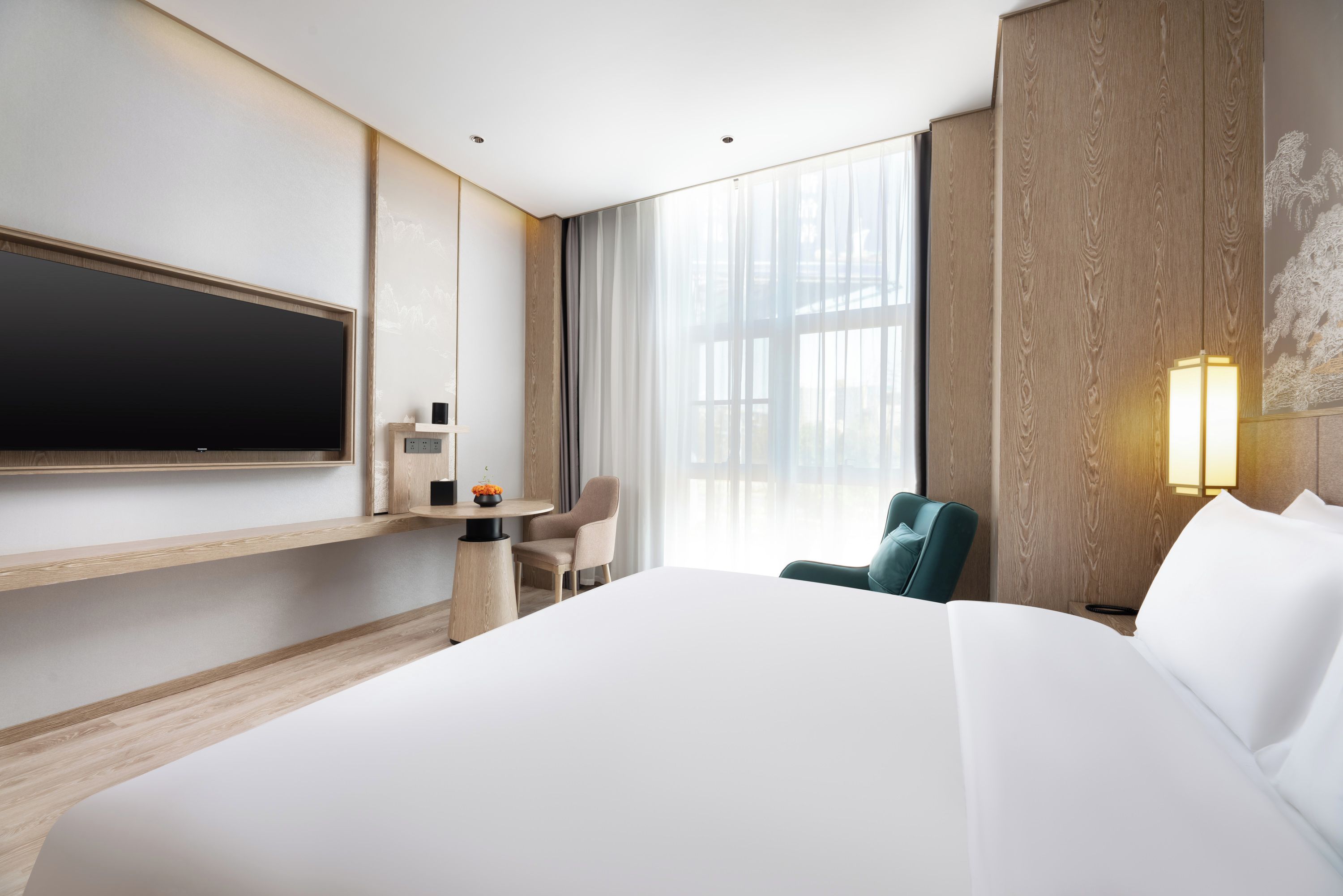 Quarto de hotel com uma cama grande, uma escrivaninha com cadeira, televisão e uma janela ampla.