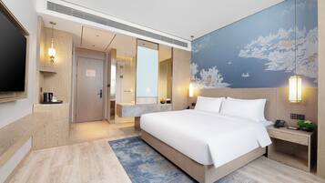 Quarto de hotel moderno com uma cama grande, televisão de tela plana, banheiro e um mural na parede.