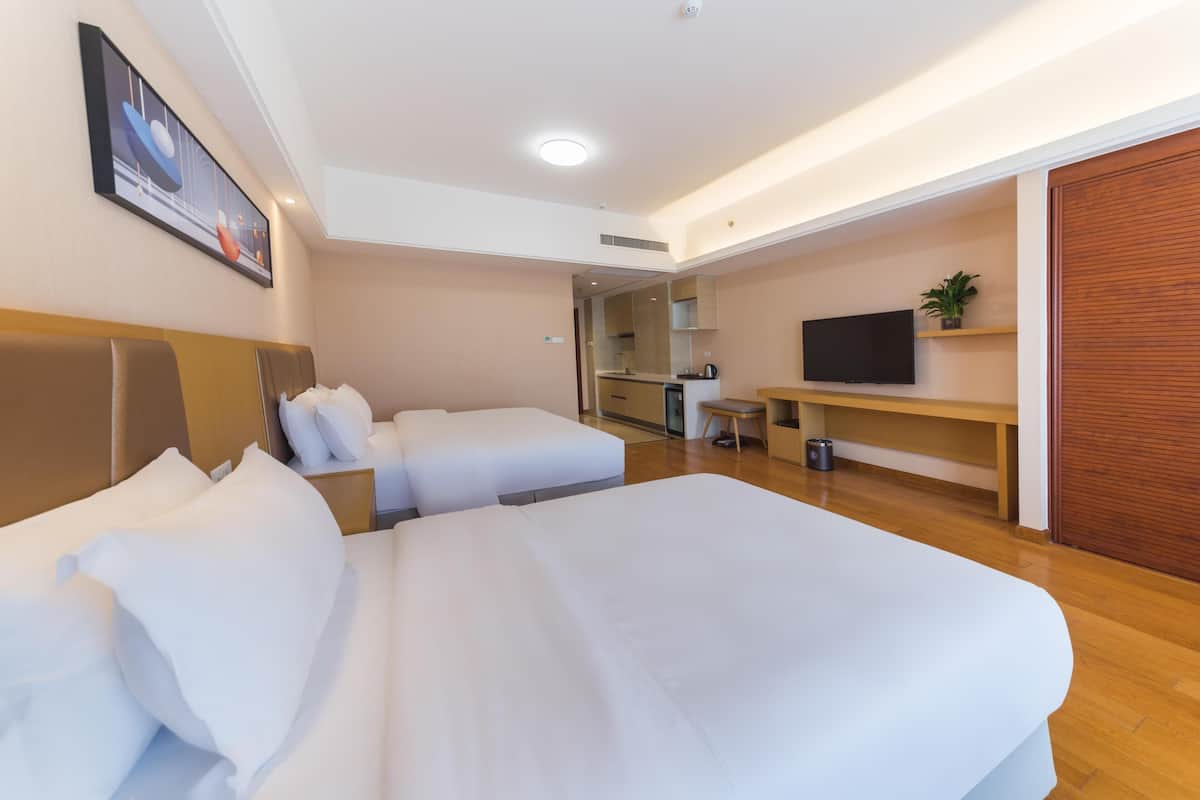 Quarto de hotel com duas camas, televisão, pequena cozinha e piso de madeira.