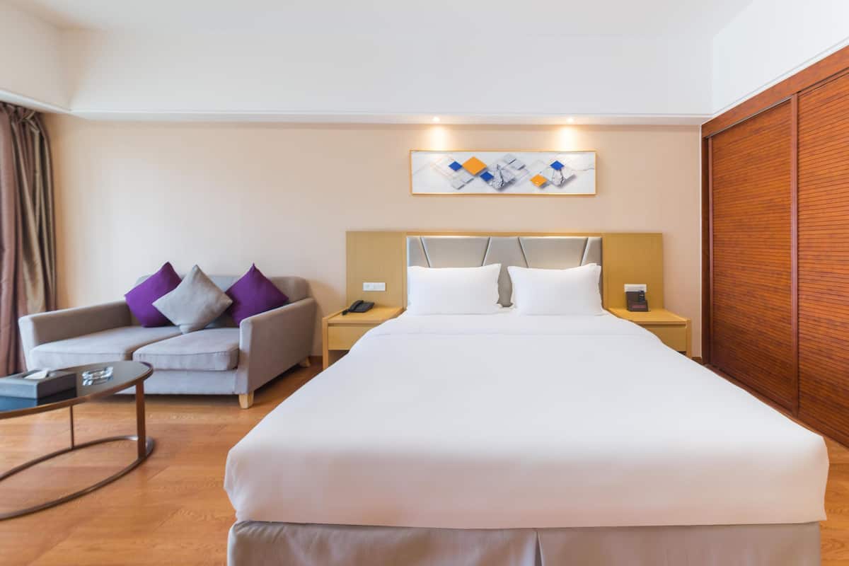 Quarto de hotel com uma cama grande, um sofá, uma mesa de cabeceira e um guarda-roupa de madeira.