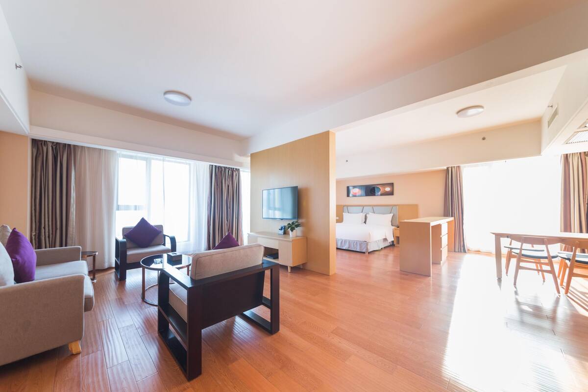 Quarto de hotel moderno com área de estar, quarto separado e área de jantar, além de uma televisão.