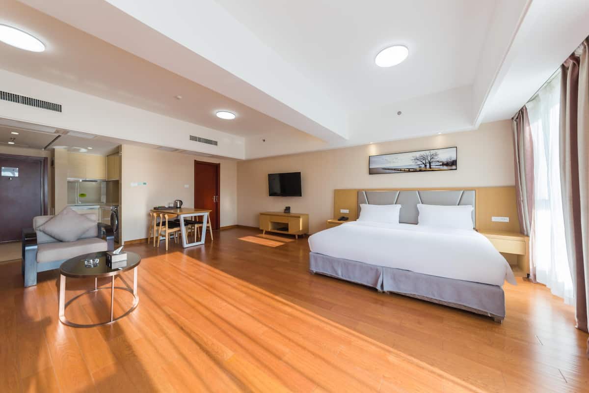 Quarto de hotel com uma cama grande, uma mesa de trabalho, um sofá, uma televisão e um quadro na parede.