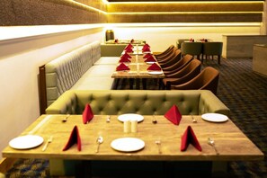 Restaurante com uma mesa comprida disposta para vários convidados, assentos acolchoados e piso coberto de carpete.