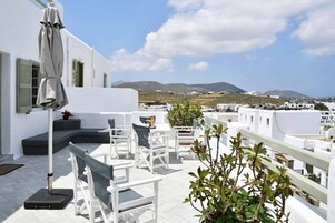 Terraço no telhado com mobiliário branco, uma planta em vaso e vista para a paisagem.