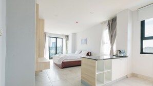 Quarto de hotel moderno com cama, cozinha compacta, janela grande e vista para a cidade.