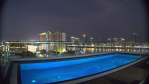 Piscina no terraço com vista para a cidade à noite.