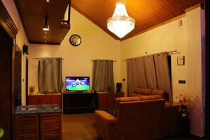 Uma sala de estar com televisão, um lustre, cortinas e um relógio na parede.