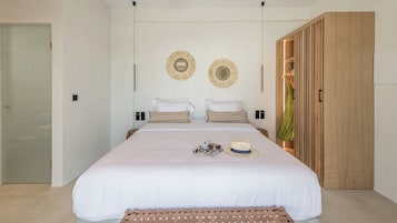 Quarto bem arrumado com cama grande, dois espelhos fixados na parede, guarda-roupa de madeira e um banquinho pequeno.
