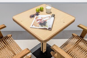 Uma mesa de madeira com uma revista, duas maçãs verdes, um copo de leite e óculos de sol.