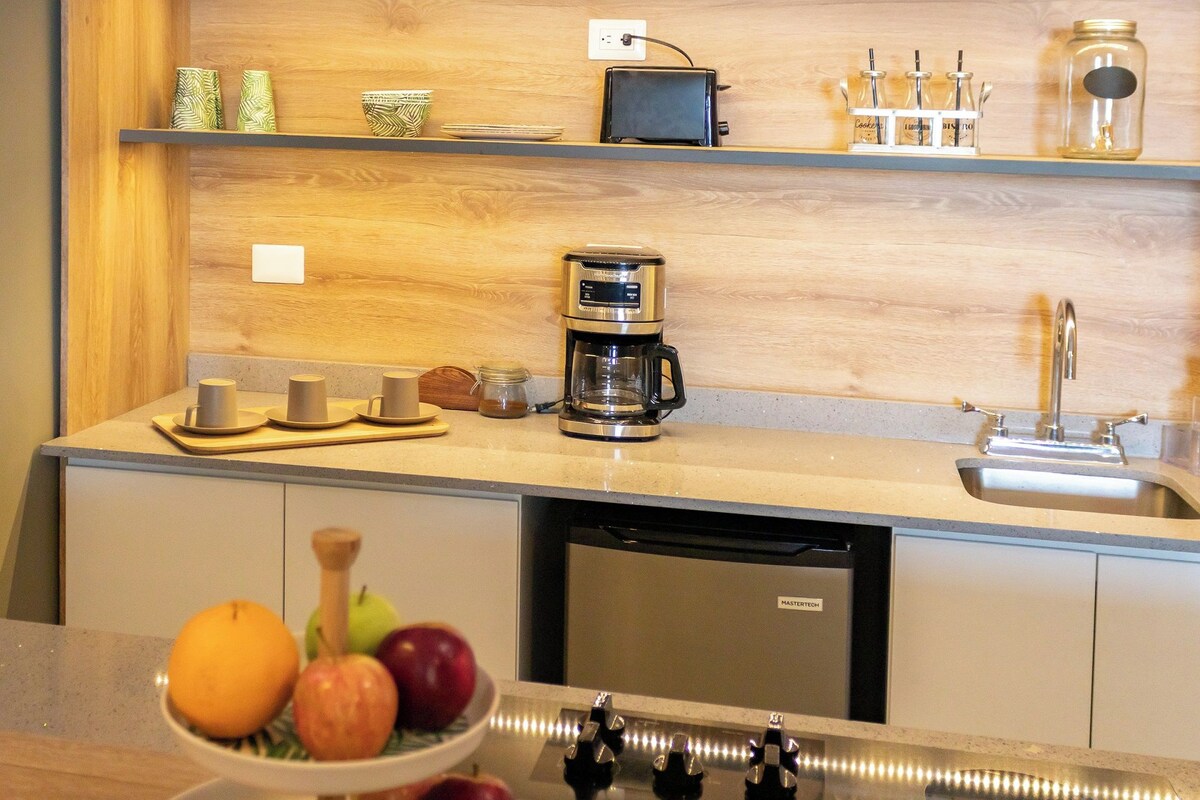 Uma cozinha com bancada de madeira, cafeteira, pia e uma fruteira.