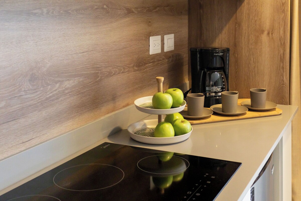 Uma cozinha com um fogão por indução moderno, uma cafeteira e uma seleção de frutas.
