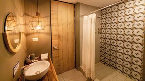 Um banheiro com porta de madeira, pia, espelho, luminária pendente e chuveiro com azulejos estampados.