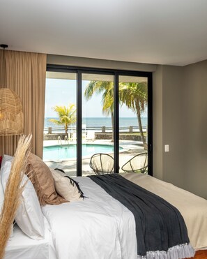 Quarto com cama, vista para uma piscina e praia, e uma janela grande.