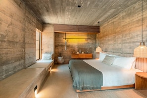 Quarto com cama, mesas de cabeceira, janela e teto de concreto.