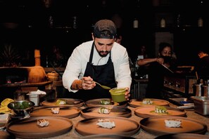 Um chef preparando comida em uma cozinha com várias travessas redondas e utensílios de cozinha.