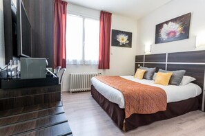 Quarto de hotel com cama, escrivaninha com um laptop, radiador e janela com cortinas.