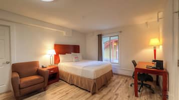 Quarto de hotel com cama, escrivaninha, cadeira, mesa de cabeceira e abajur.
