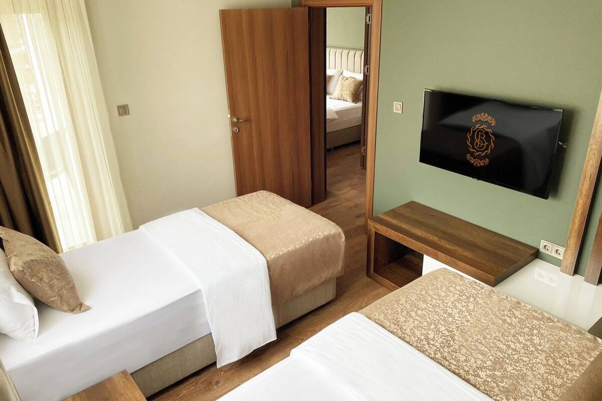 Quarto de hotel com duas camas, uma televisão e uma porta de madeira que dá para outro quarto.