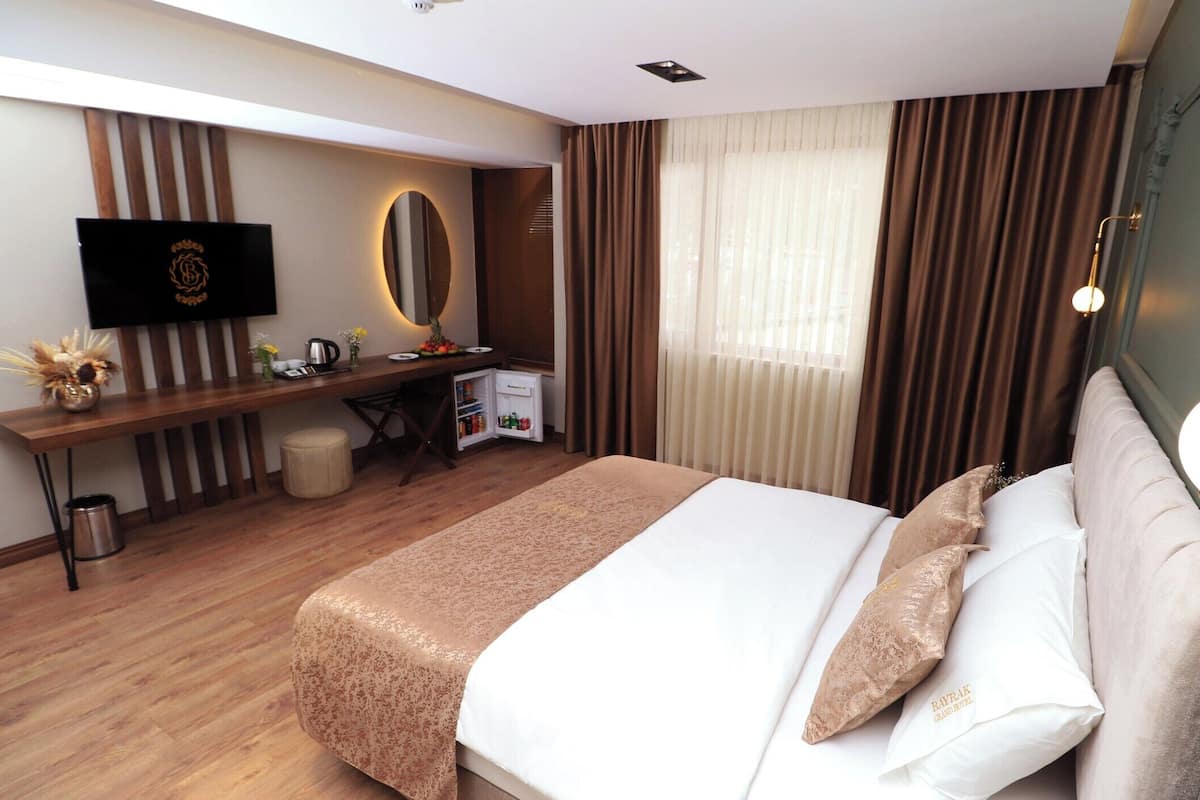 Quarto de hotel com cama, escrivaninha, televisão, minibar e banheiro.