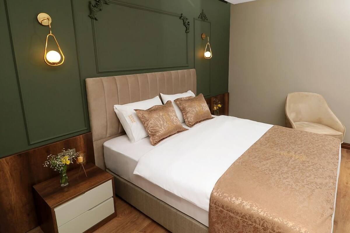 Cama bem arrumada com cabeceira, mesa de cabeceira com um vaso de flores e uma cadeira.
