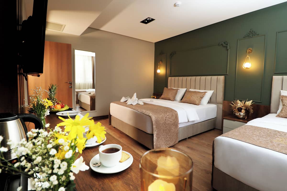 Quarto de hotel com duas camas, área de refeições com flores, espaço para café e televisão.