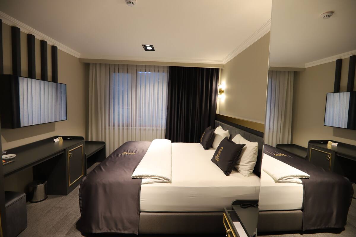 Quarto de hotel com uma cama grande, televisão, escrivaninha e espelho.
