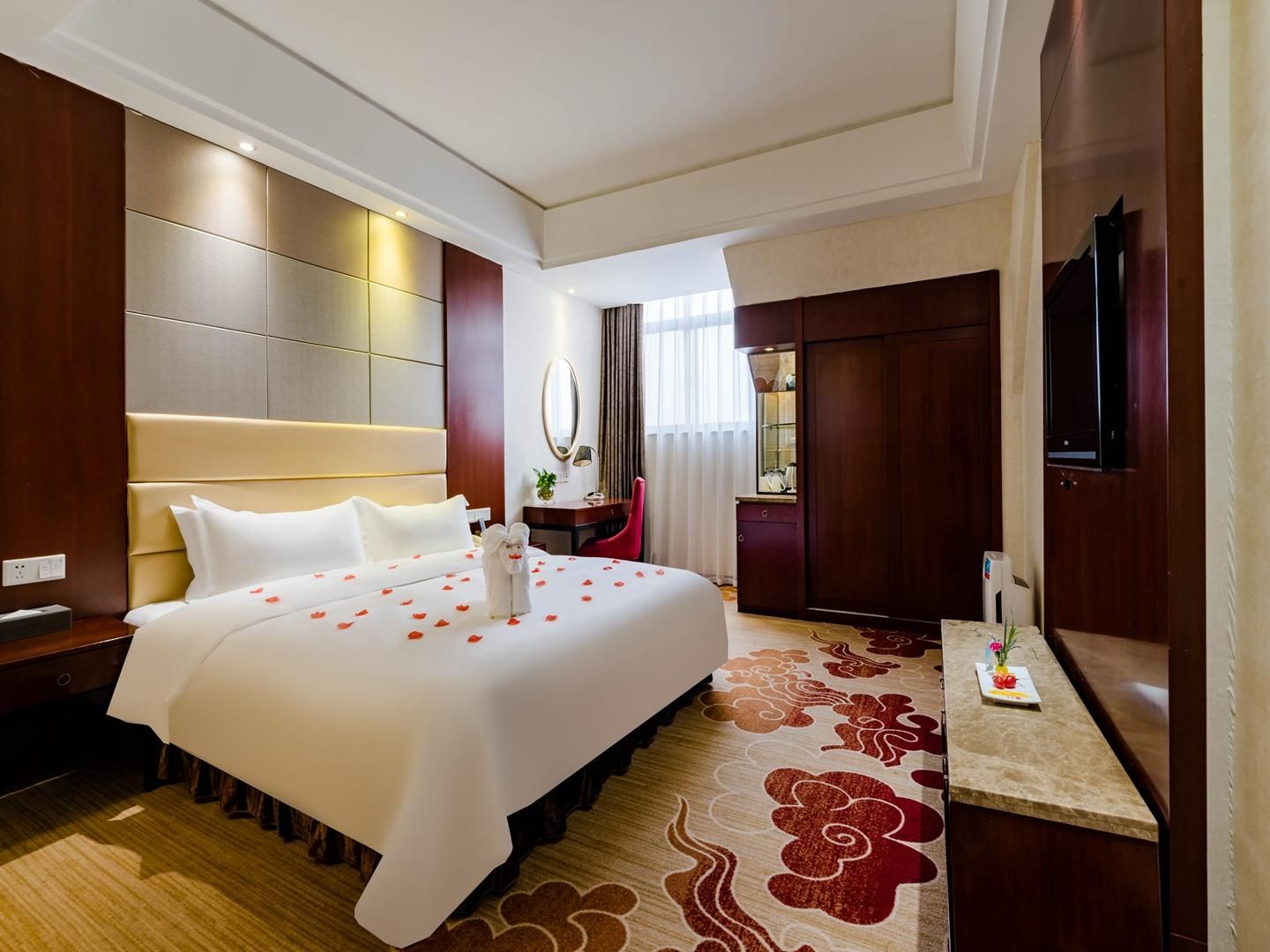 Quarto de hotel com cama grande, mesa de cabeceira, espelho, televisão e escrivaninha com cadeira.