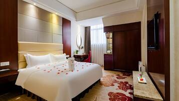 Quarto de hotel com cama grande, mesa de cabeceira, espelho, televisão e escrivaninha com cadeira.