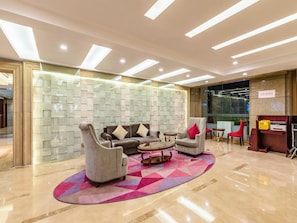 Um hall com sofás, uma mesa de centro, parede estampada e um balcão de recepção.