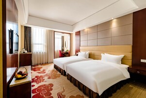 Quarto de hotel com duas camas, uma escrivaninha com uma cesta de frutas, televisão e um espelho grande.