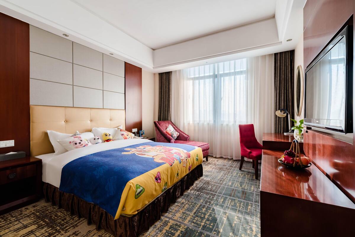 Quarto de hotel com uma cama grande, uma escrivaninha, uma cadeira e uma televisão.