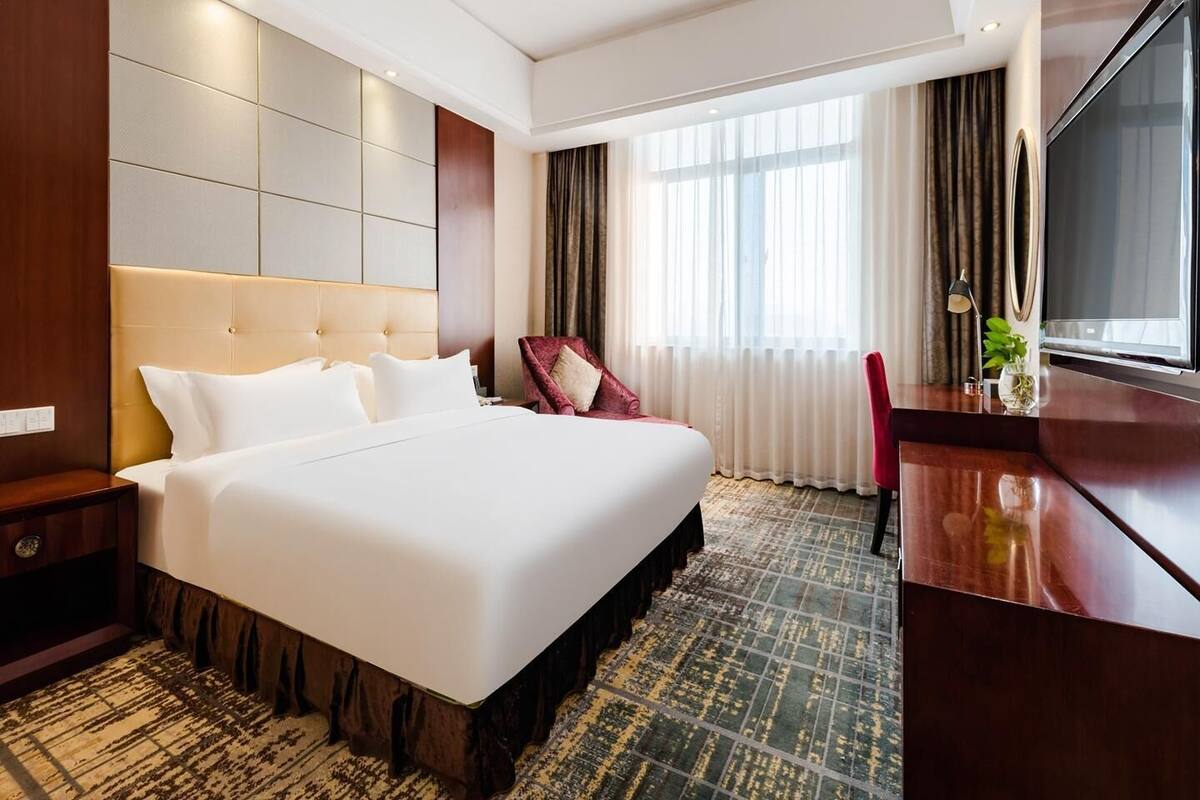 Quarto de hotel com uma cama grande, uma escrivaninha, uma cadeira e uma televisão.