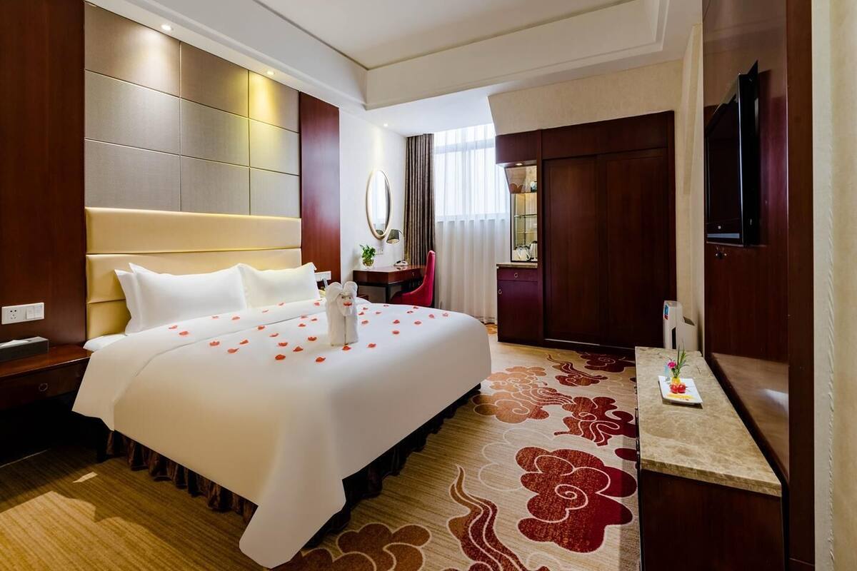 Quarto de hotel com cama grande, mesa de cabeceira, espelho, televisão e escrivaninha com cadeira.