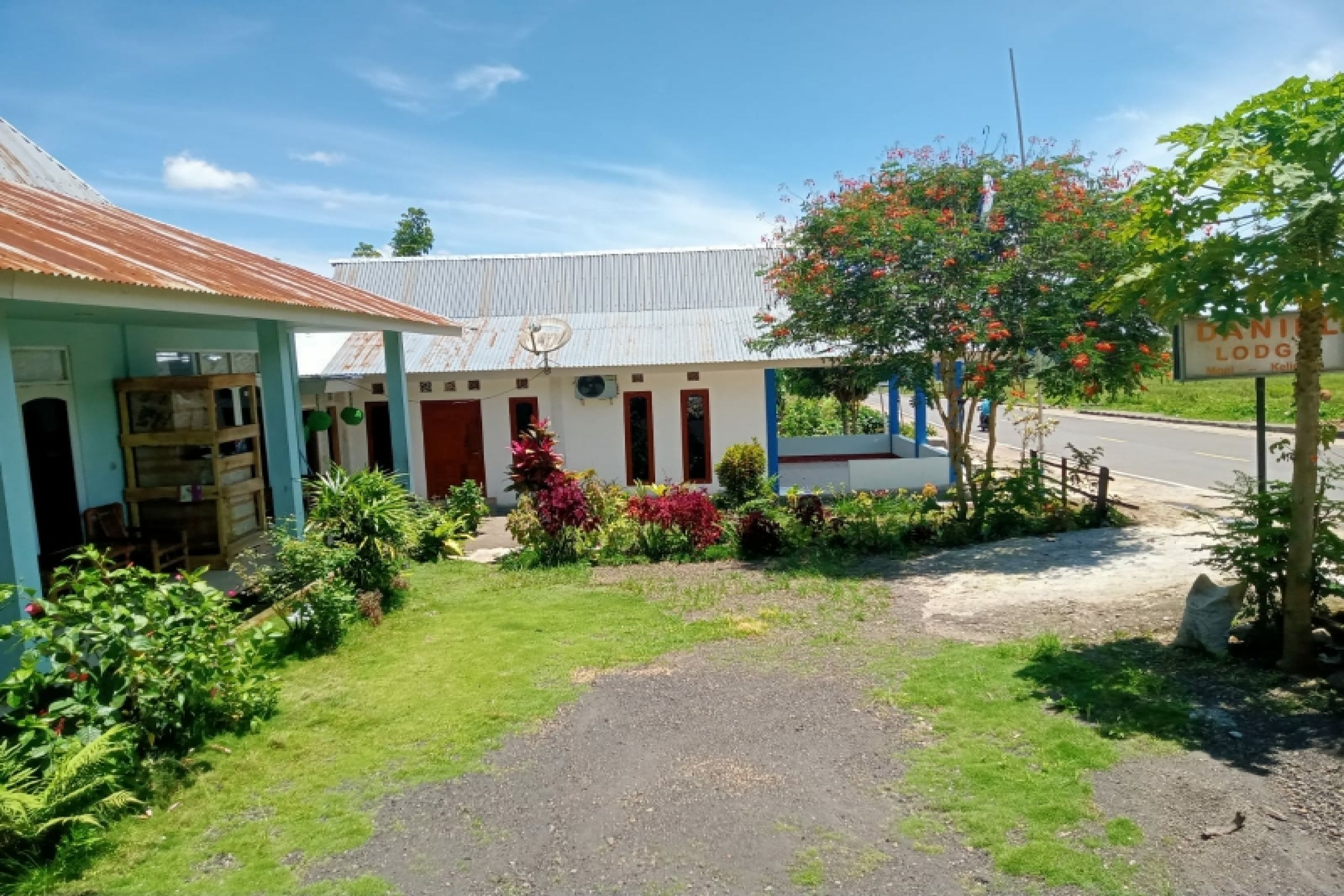 Um edifício com telhado de metal corrugado, uma placa e um jardim bem cuidado com várias plantas e flores.