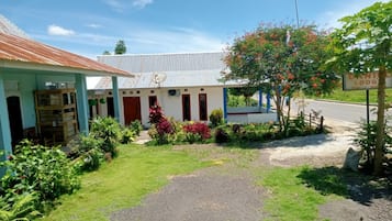 Um edifício com telhado de metal corrugado, uma placa e um jardim bem cuidado com várias plantas e flores.
