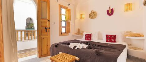 Quarto com cama, um banco de madeira, varanda e vista para o exterior.