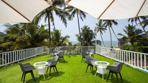 Terraço com área de estar ao ar livre, palmeiras e vista para o oceano.