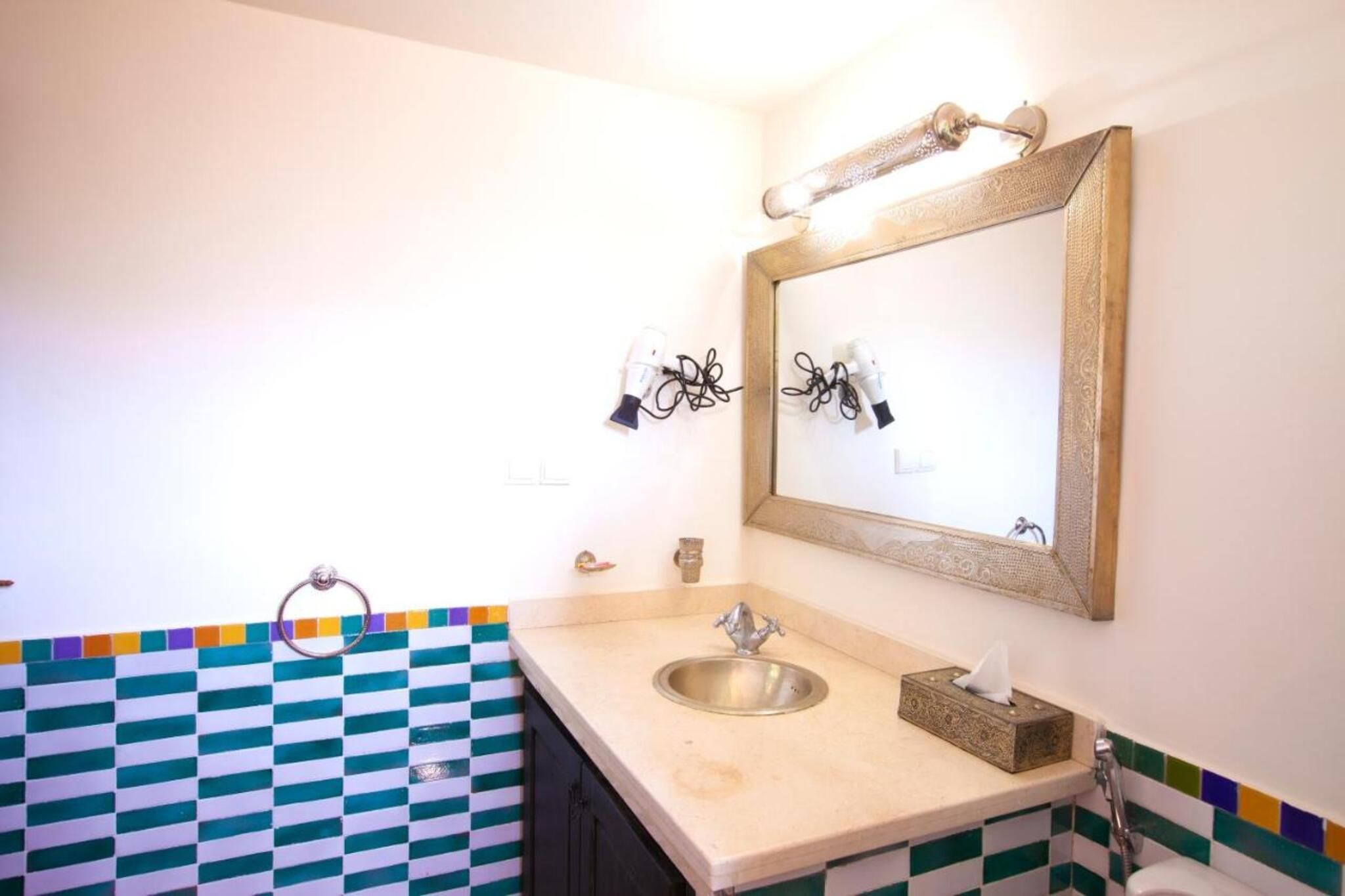 Um banheiro com detalhes em azulejos xadrez, pia com espelho e porta-toalhas.