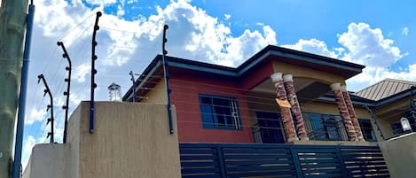 Edifício residencial com entrada gradeada, varanda e céu aberto.
