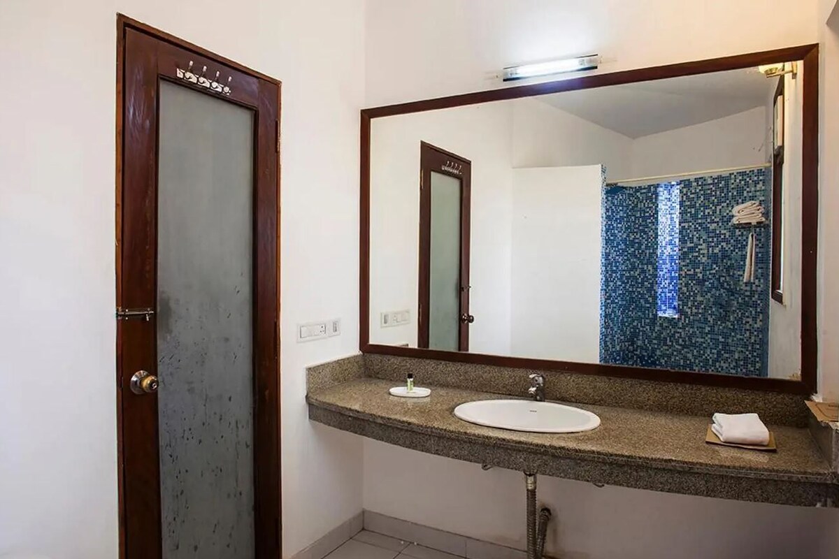 Casa de banho com porta de madeira, pia com espelho em cima e área de duche com parede em mosaico azul.