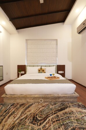 Quarto com uma cama grande, cabeceira de madeira, janela com persianas, mesa de cabeceira com luminária e ar-condicionado fixado na parede.