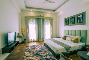 Quarto com cama, televisão, escrivaninha, cadeira, ventoinha no teto e janela com cortinas.